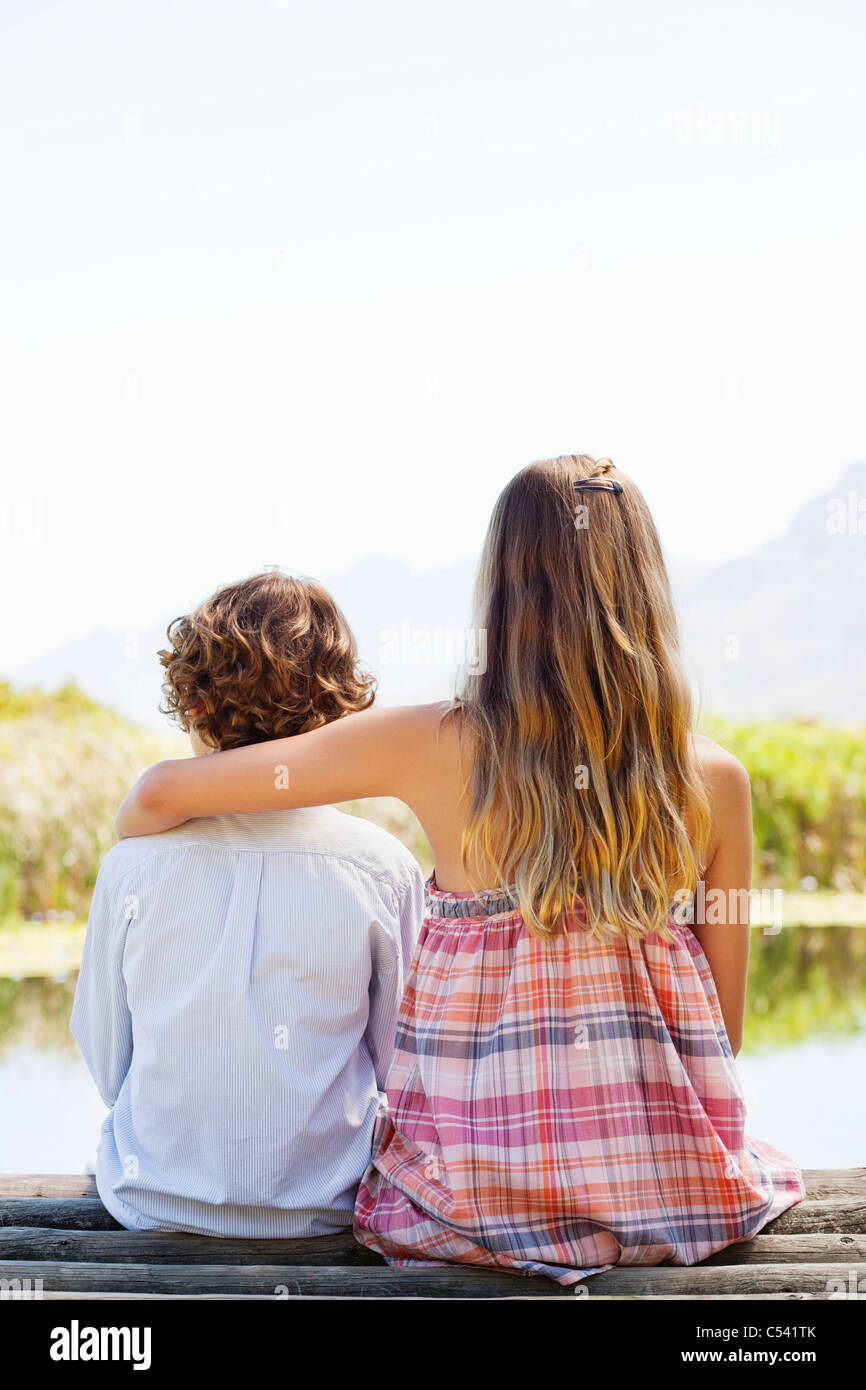 Rear view of siblings sitting together at a pier Stock Photo - Alamy