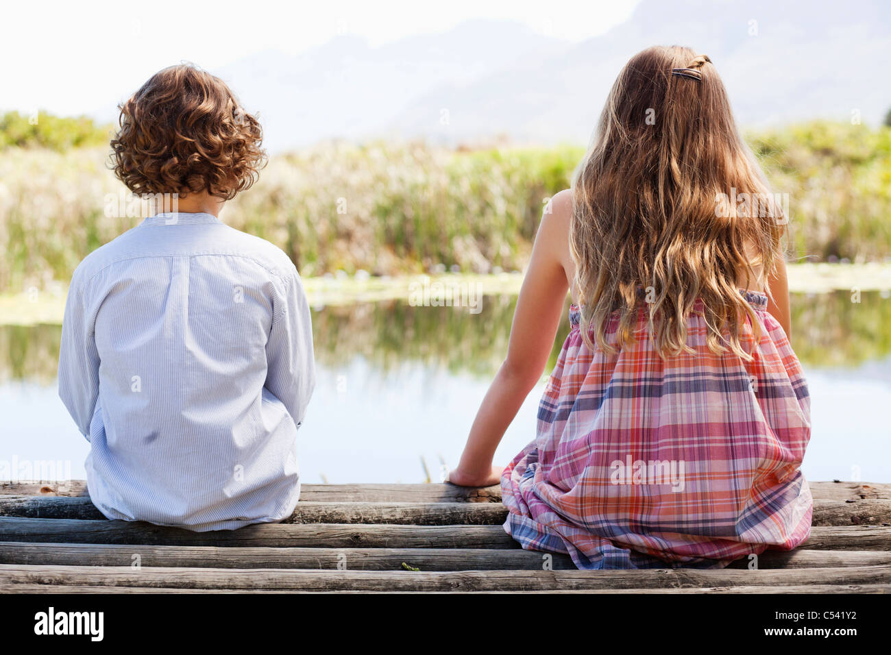 Rear view of siblings sitting together at a pier Stock Photo - Alamy