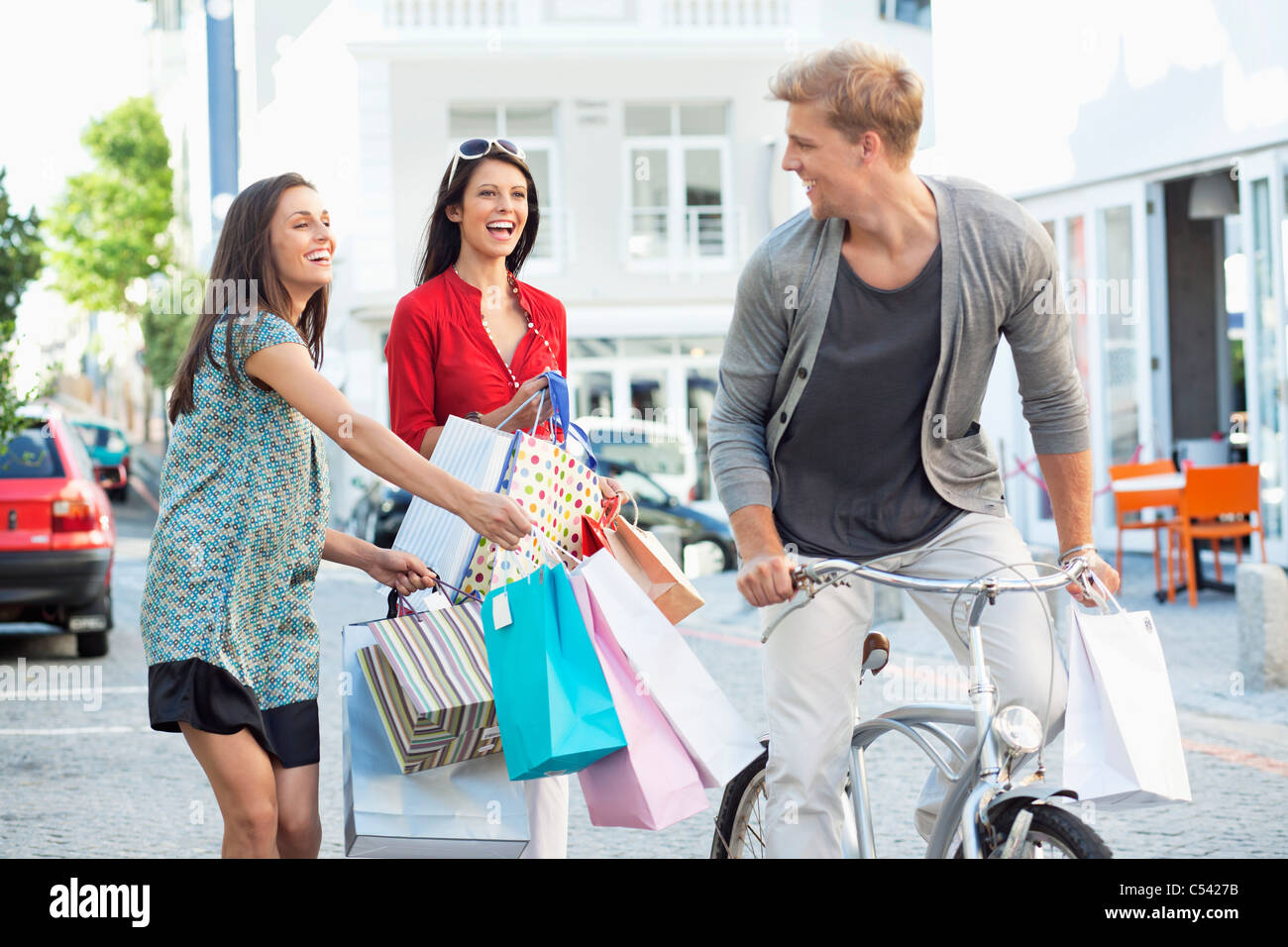 Young man cycling with two women running after him with shopping bags ...