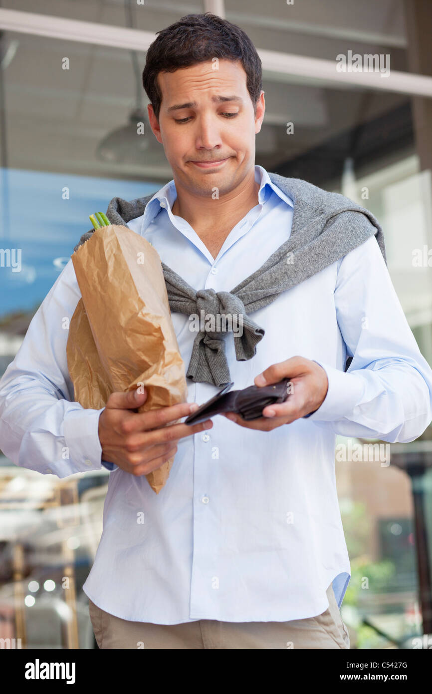Mid adult man checking the empty wallet with paper bag full of ...
