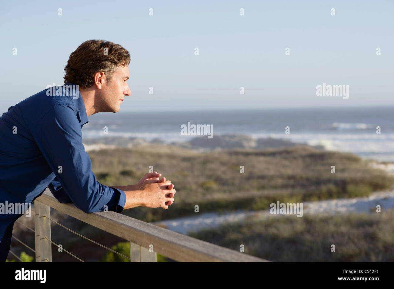 Mid adult man leaning on a railing of a balcony Stock Photo - Alamy
