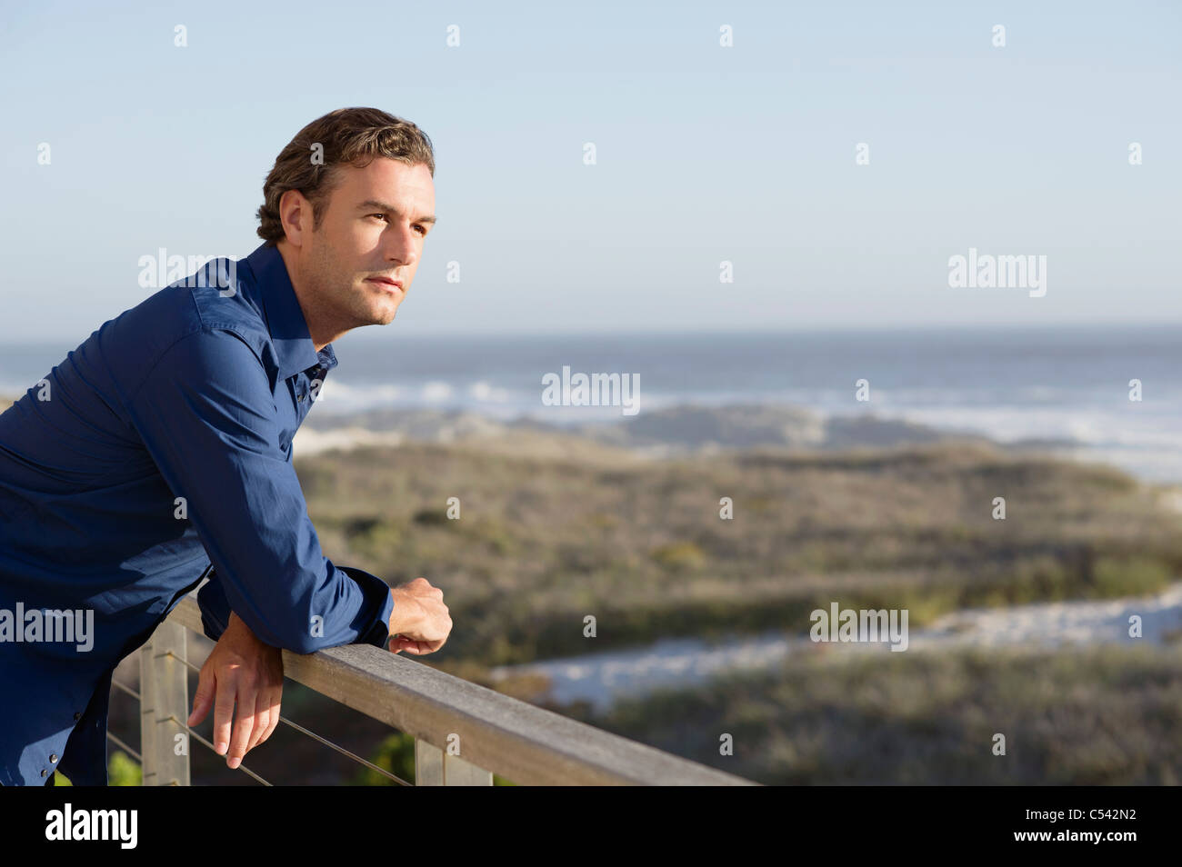 Mid adult man leaning on a railing of a balcony Stock Photo - Alamy