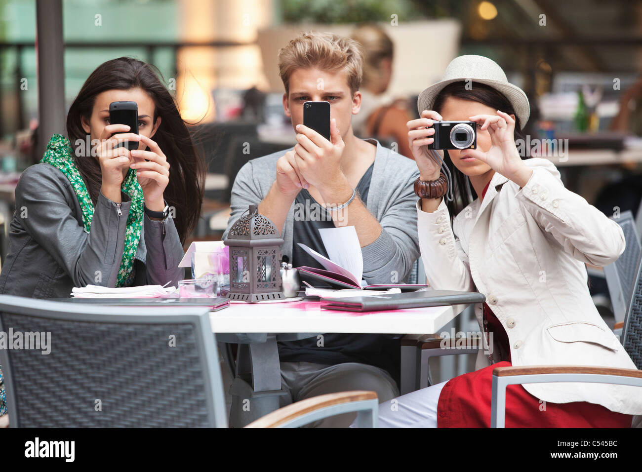 Three young friends using electronic gadgets in a restaurant Stock ...