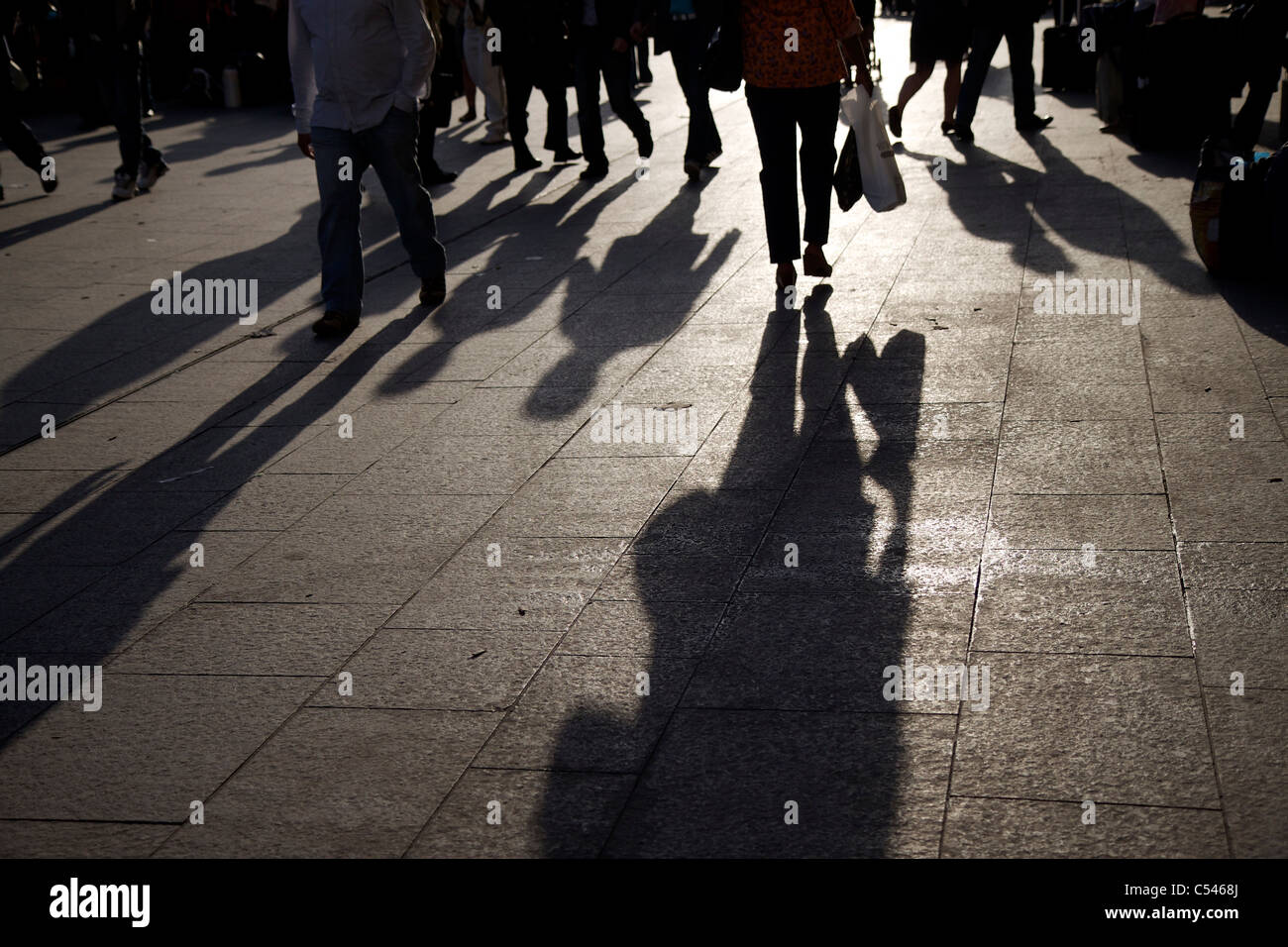 Busy commuters rush along street throwing long shadows onto the ...