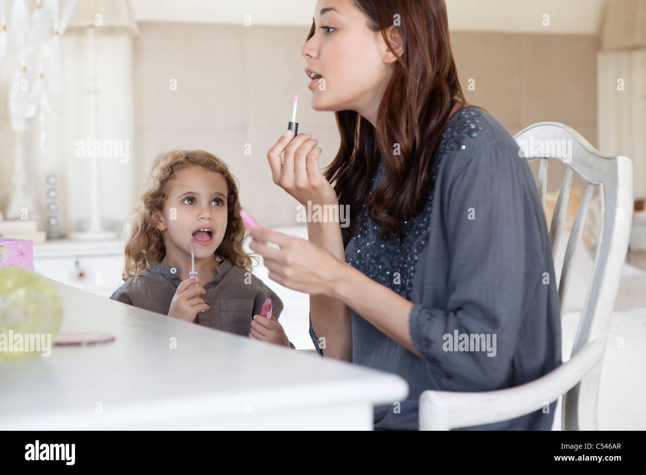 Young woman and little girl applying lip gloss at dressing table Stock ...