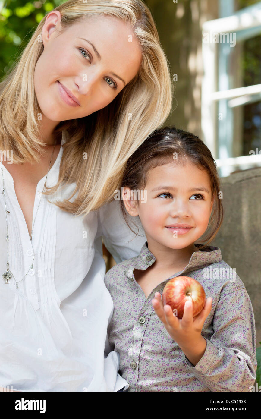 Daughter holding apple with mother smiling Stock Photo - Alamy