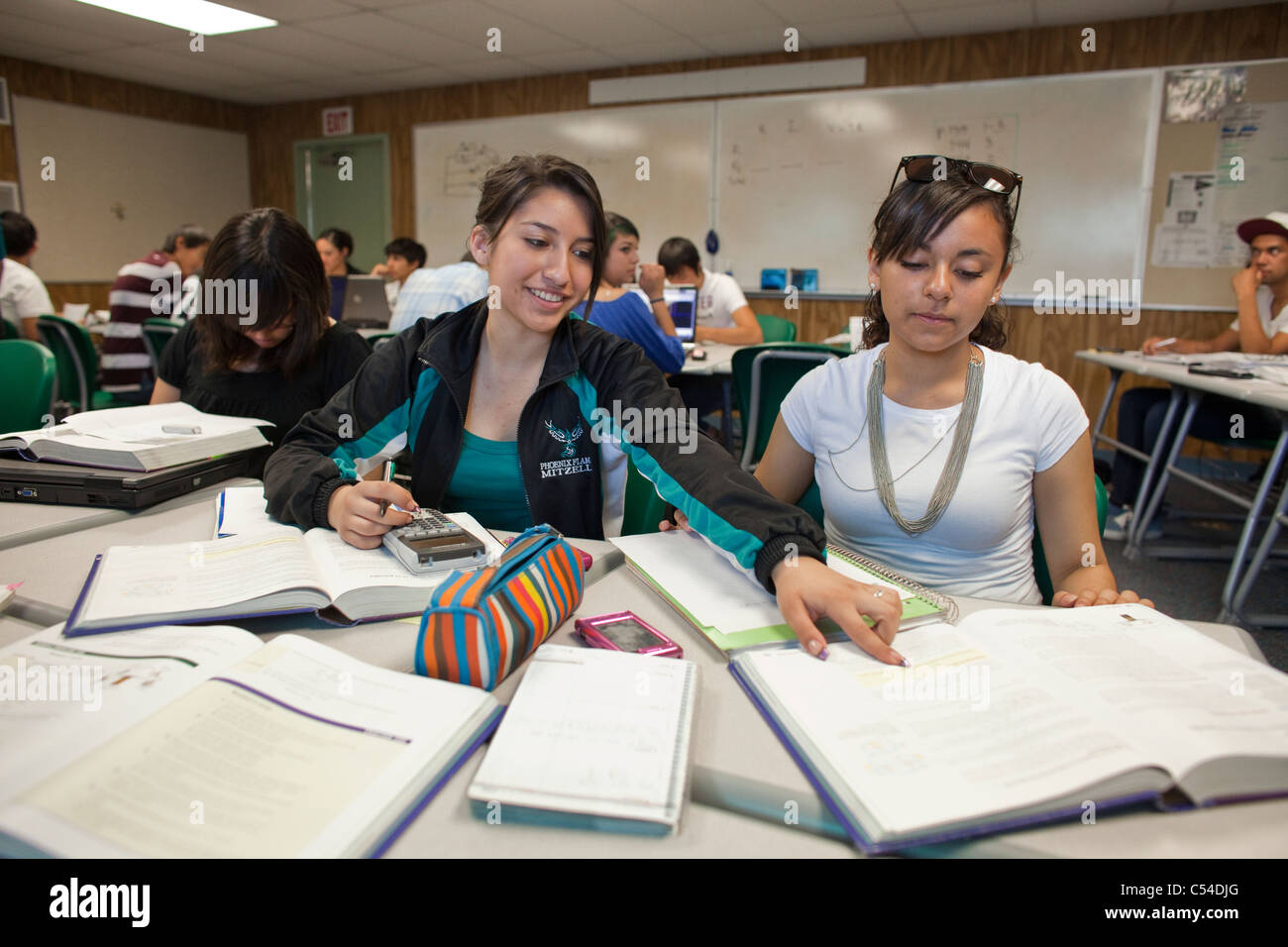 Hispanic teen female student helps fellow student by points to textbook ...