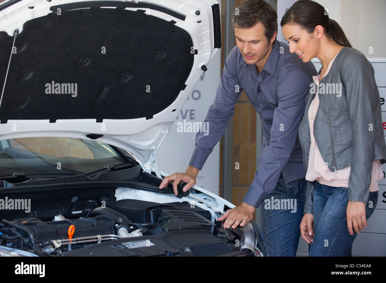 Couple looking at car engine in showroom Stock Photo - Alamy