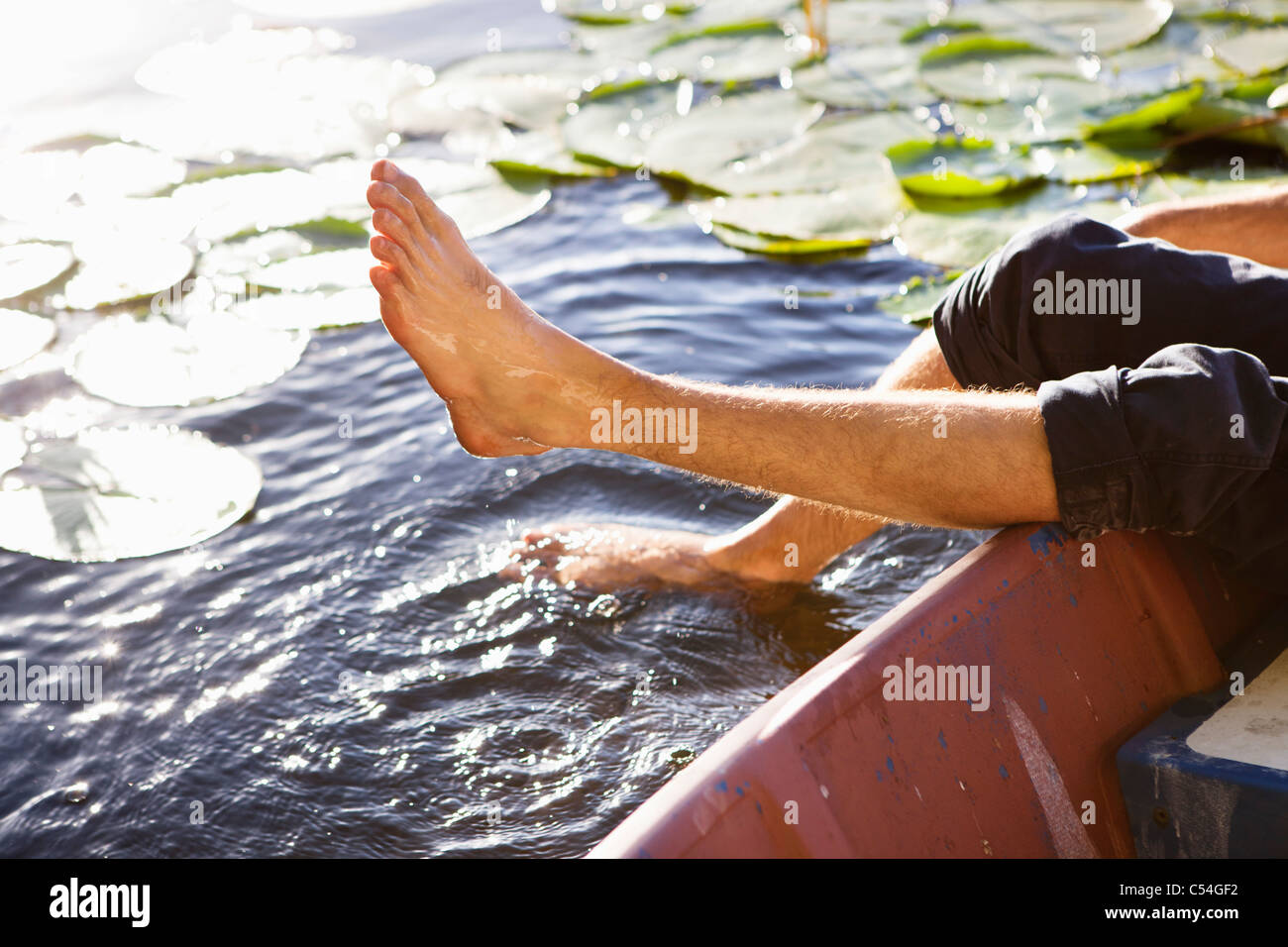 Man lying in a boat and dipping his legs in a pond Stock Photo - Alamy