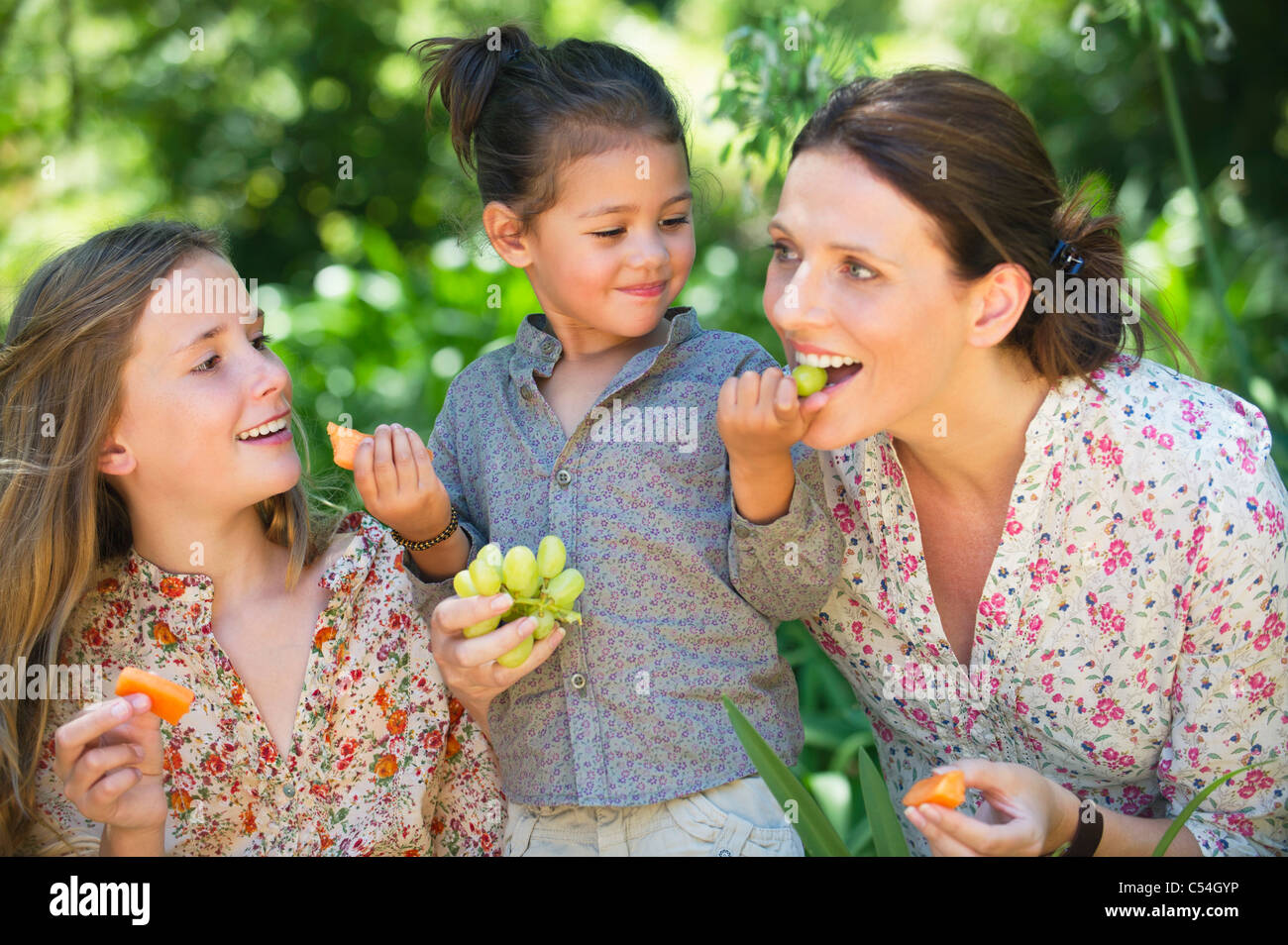 Happy mother eating fruits with her two daughters outdoors Stock Photo ...