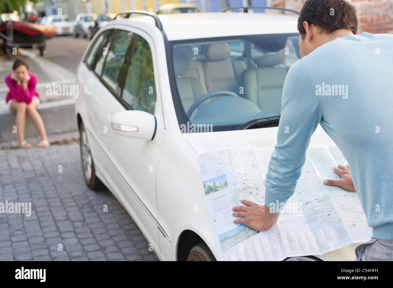 Rear view of a man looking at map on car with young woman sitting in ...