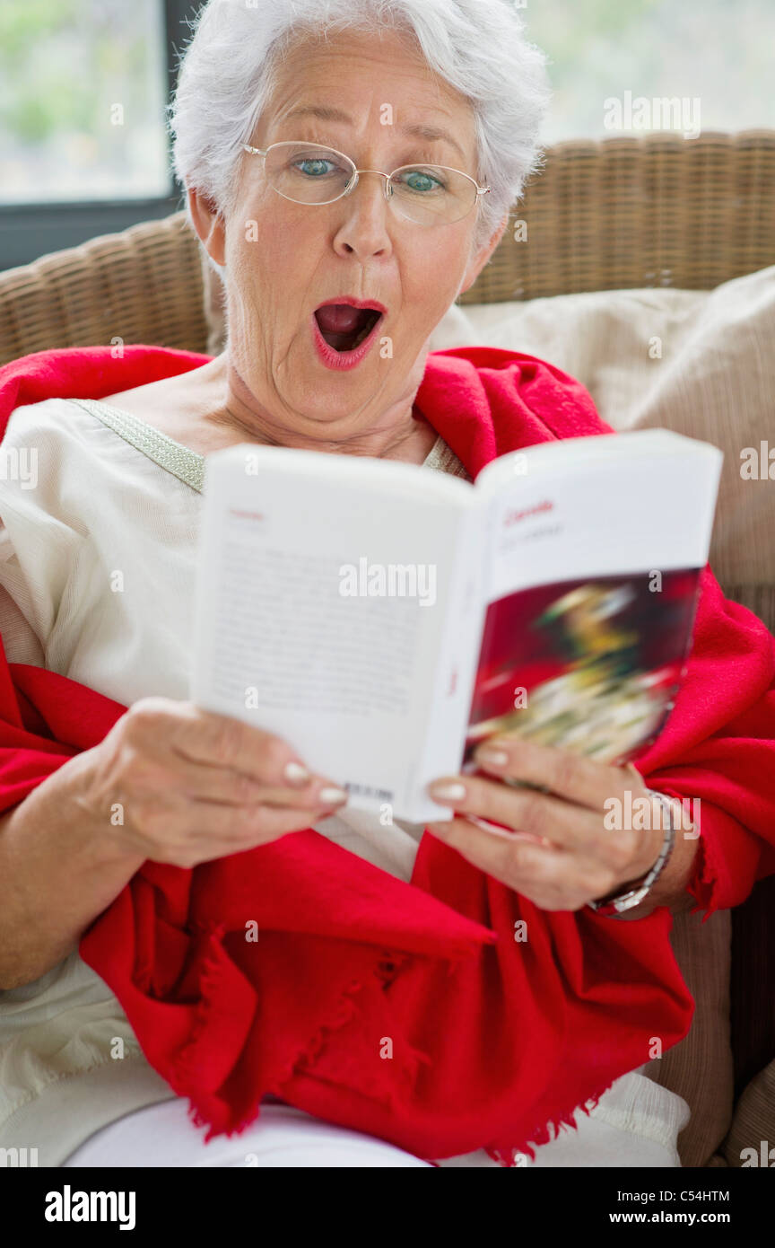 Senior woman reading a magazine and looking surprised Stock Photo - Alamy