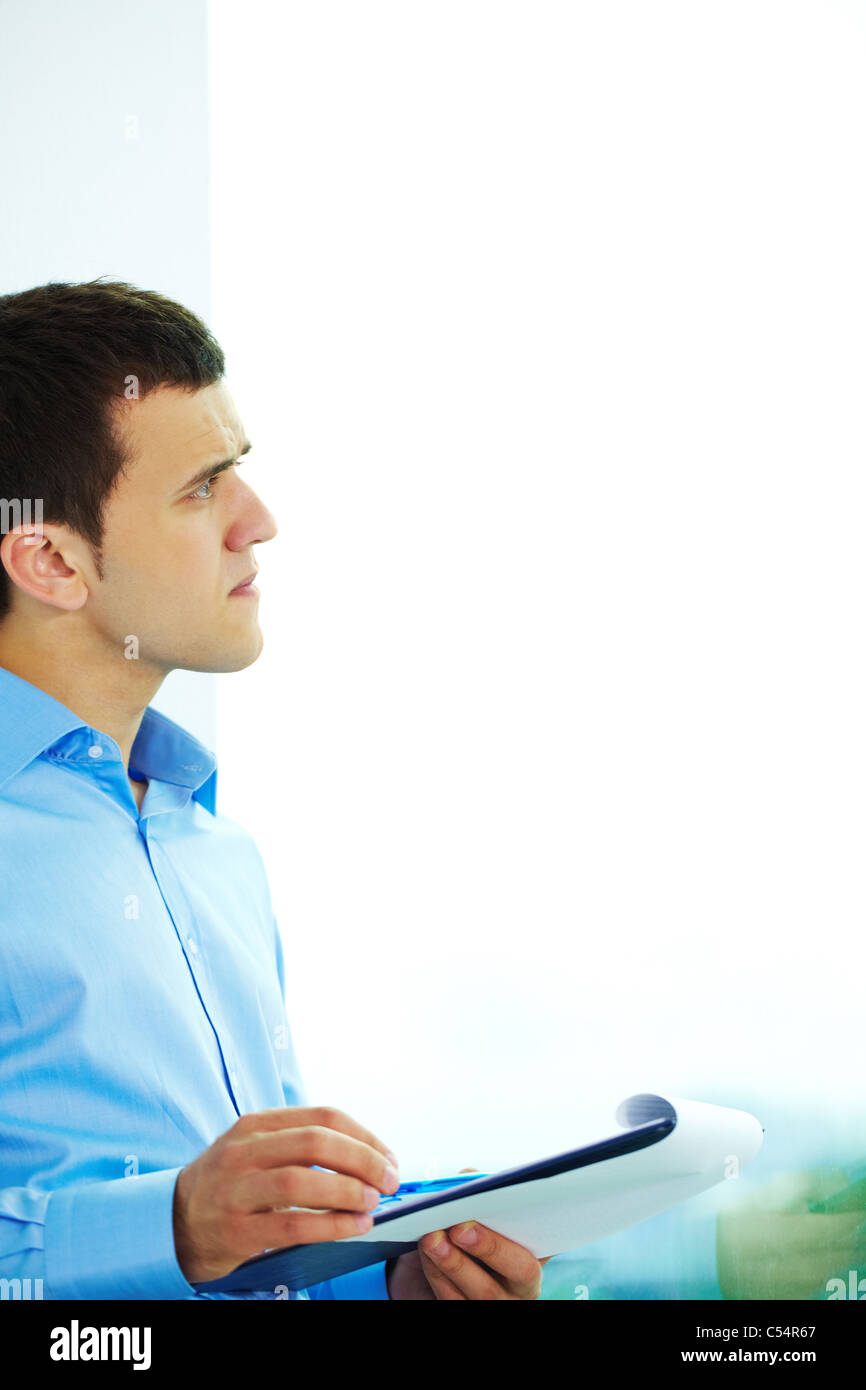 Portrait of pensive man with plan looking through window in office ...