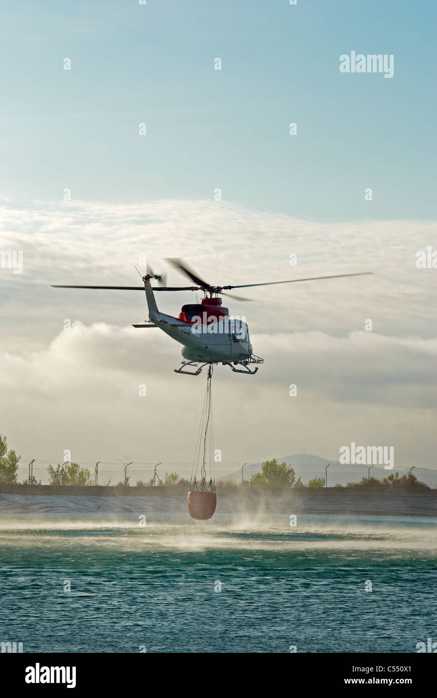 Fire brigade helicopter hovering over water while refilling the tank ...