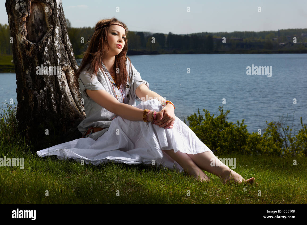 outdoor portrait of beautiful hippie girl sitting near birch. lake and ...