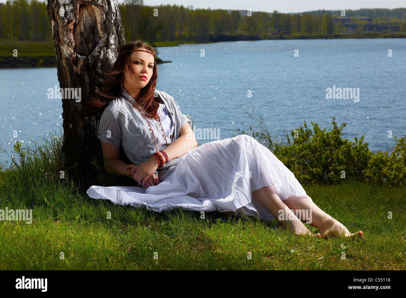 outdoor portrait of beautiful hippie girl sitting near birch. lake and forest on background ...