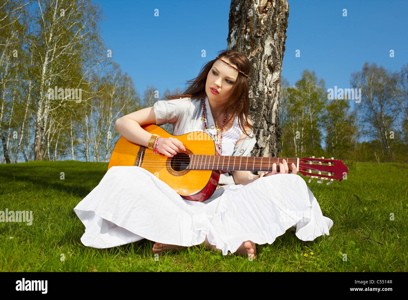 outdoor portrait of beautiful hippie girl sitting near birch on green ...