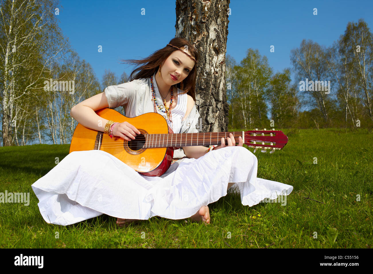outdoor portrait of beautiful hippie girl sitting near birch on green grass with guitar Stock ...