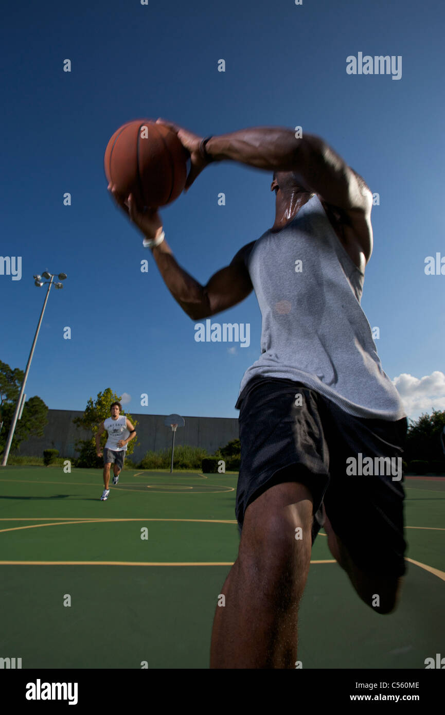 males playing outdoor street basketball with one player driving to ...