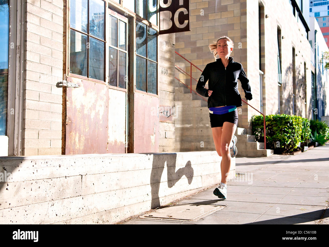 Female athlete running on sidewalk, Midtown, San Diego, California, USA ...