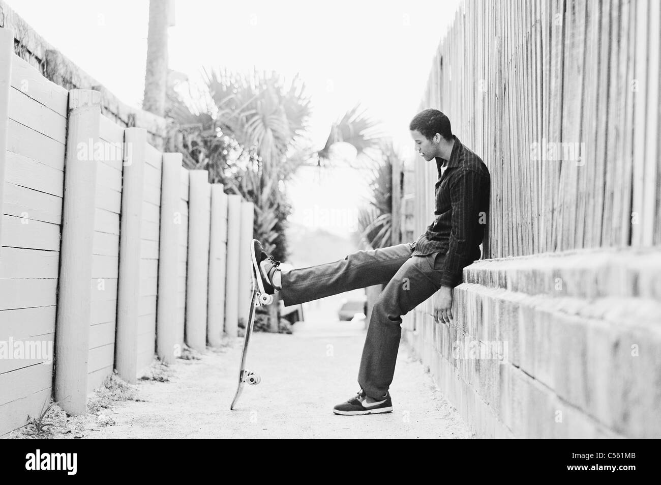 Young man sitting on a wall and playing with a skateboard Stock Photo ...