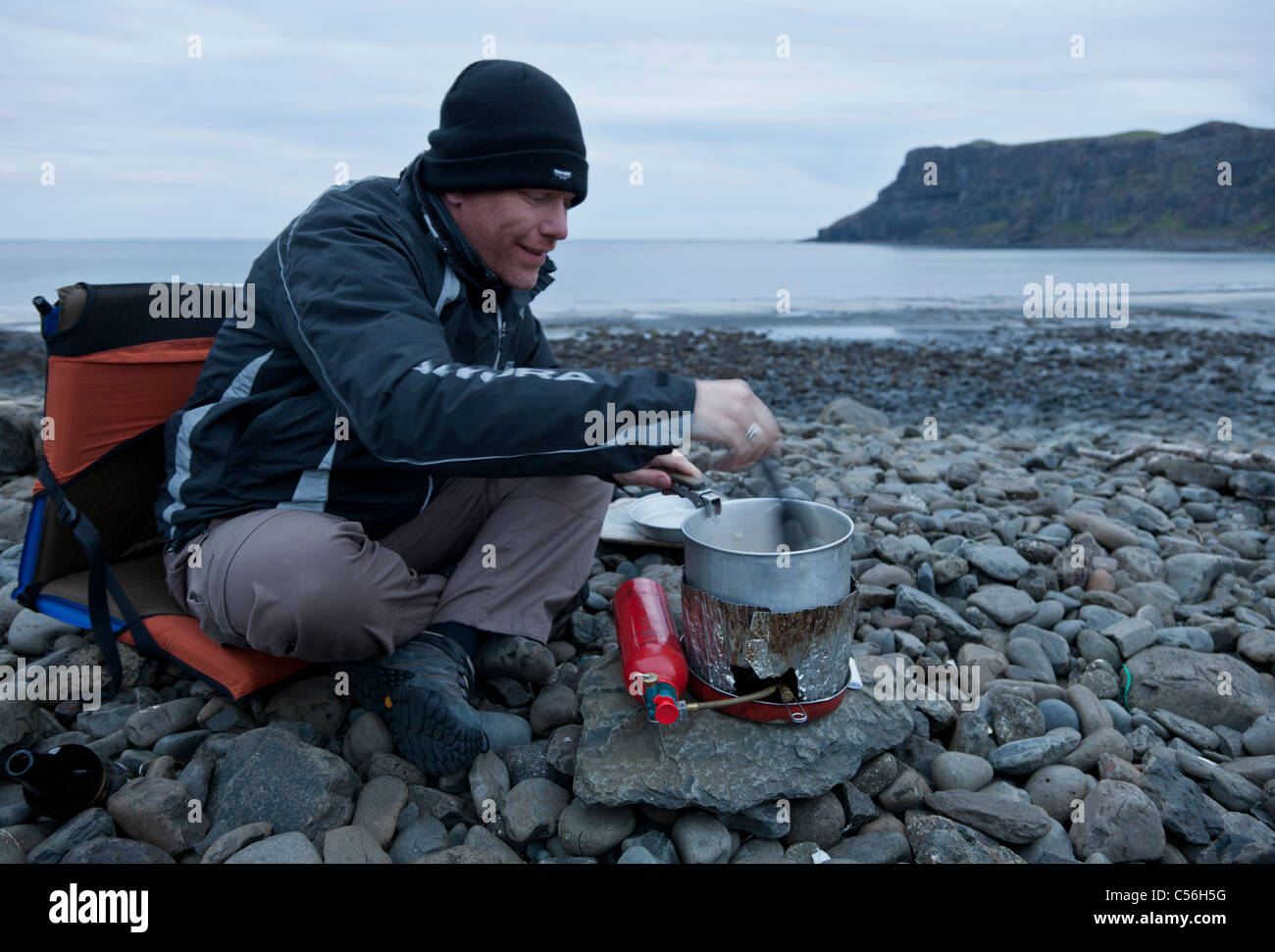 Man stirring a pot while camp cooking on a shingle beach, Talisker Bay ...