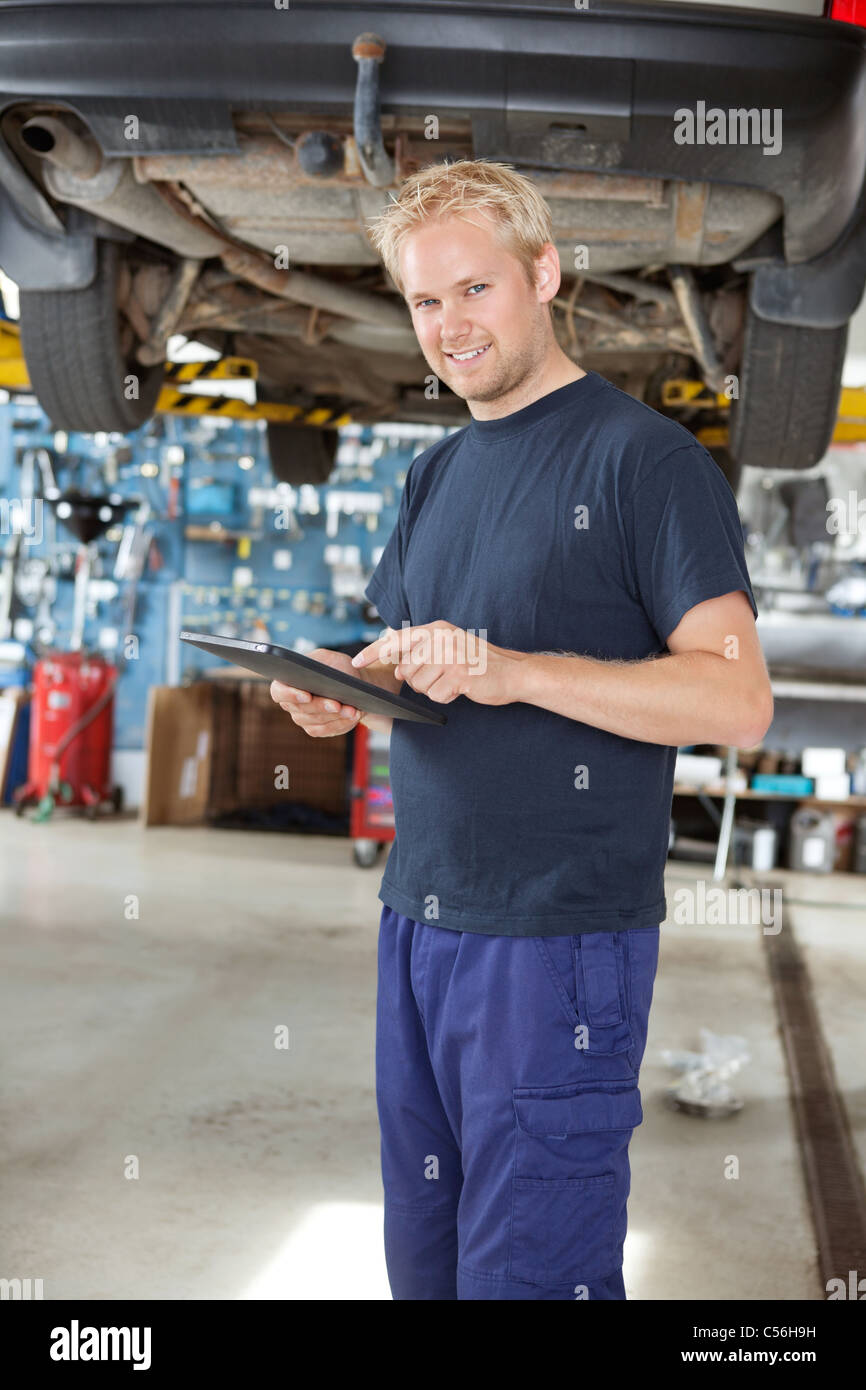 Portrait of young mechanic standing and using digital tablet in his ...
