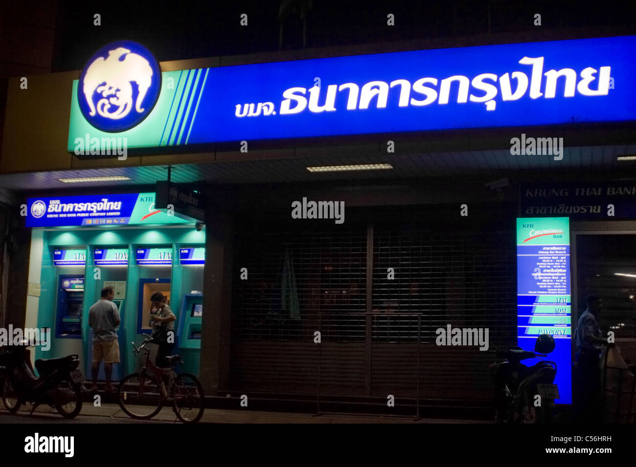 People are using an ATM machine at night at a bank in a city in ...