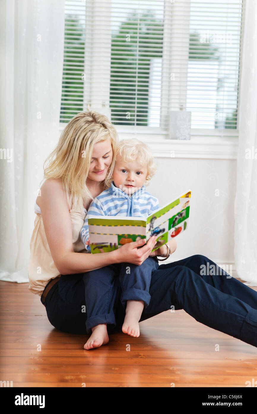 Mother and baby reading book while sitting on floor Stock Photo - Alamy