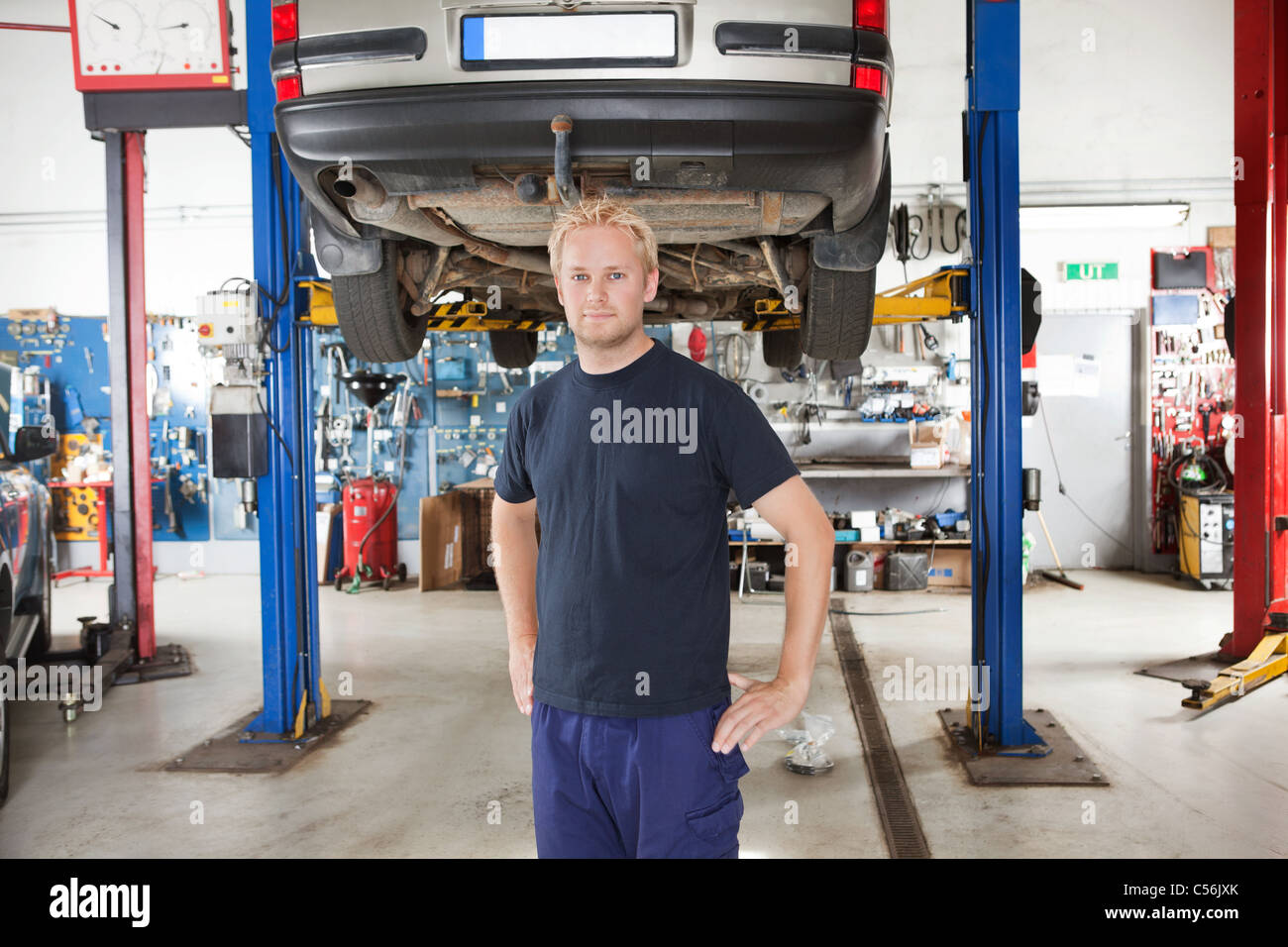 Portrait of smiling young mechanic standing inside his auto repair shop ...
