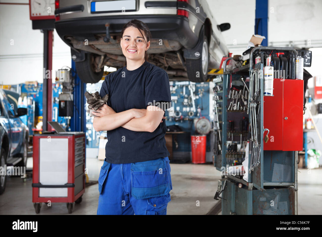 Portrait of smiling young female mechanic with arms crossed in auto ...