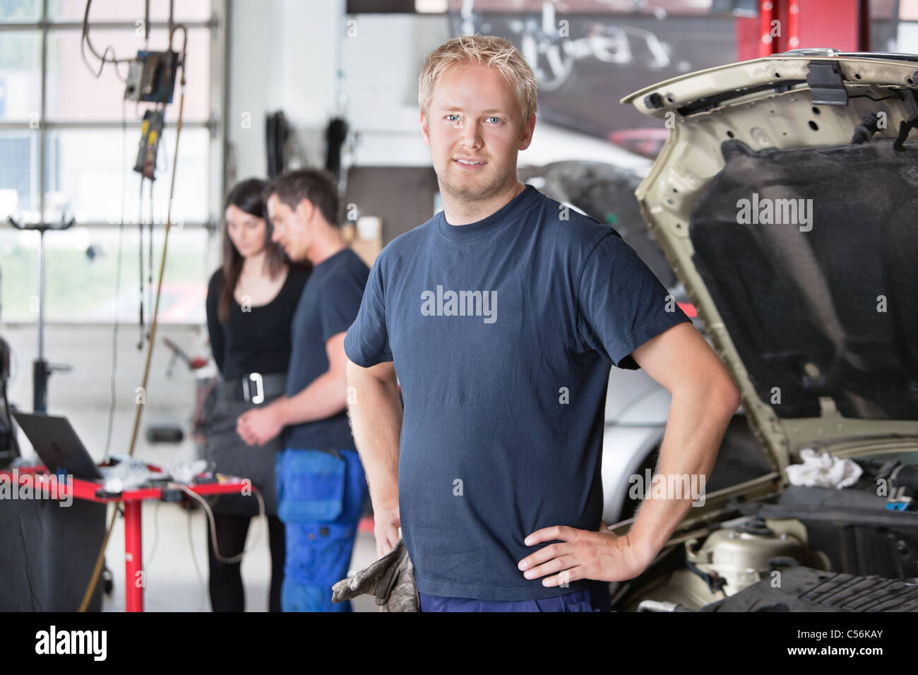 Portrait of a young mechanic in auto repair shop with customer in ...
