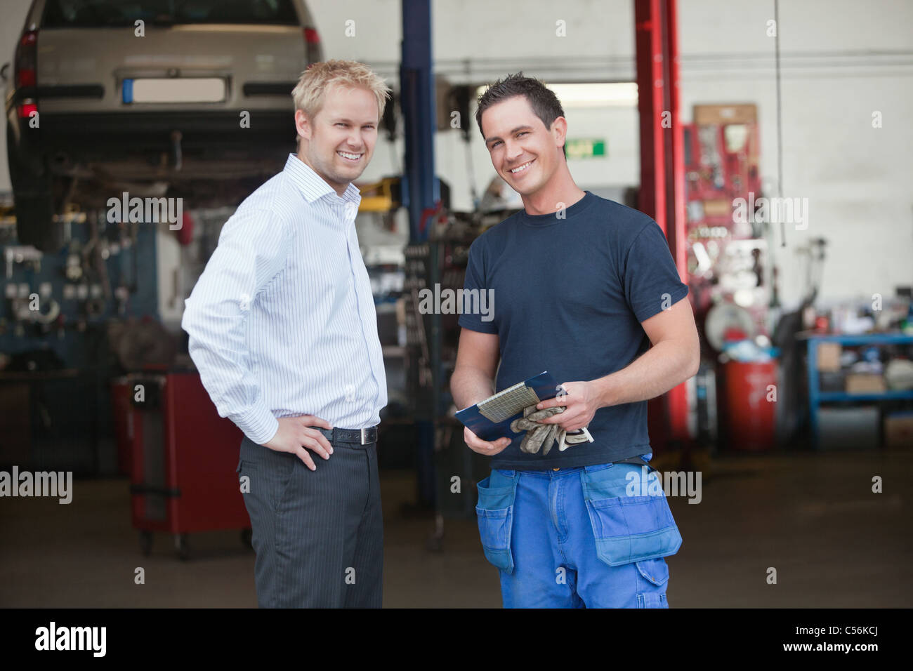 Portrait of a male customer standing with mechanic outside the garage ...