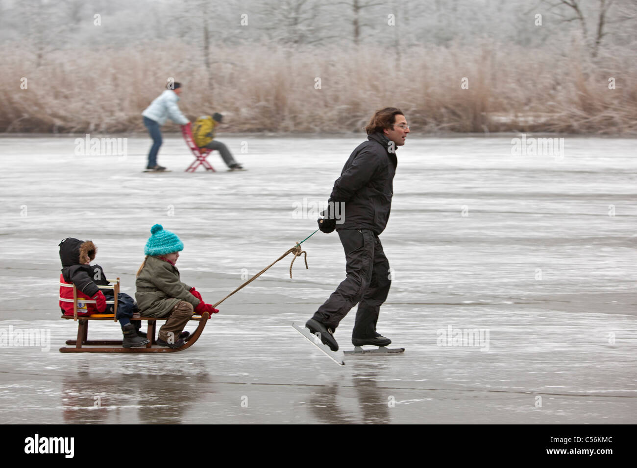 The Netherlands, Ankeveen. Man and two children on sledge ice skating ...
