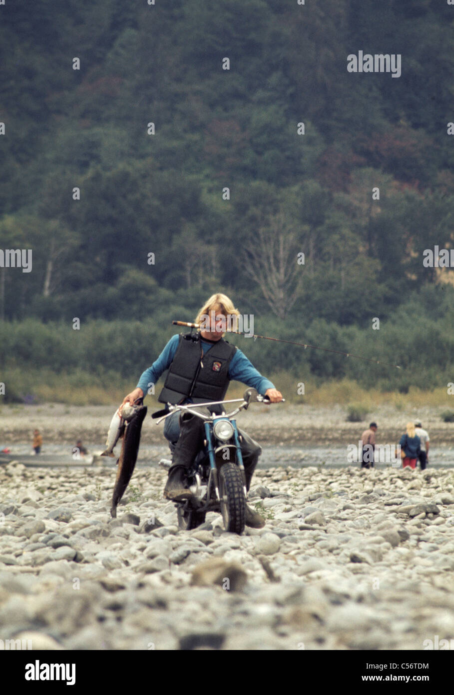 fisherman with rod in mouth and Steelhead Salmon in hand rides ...