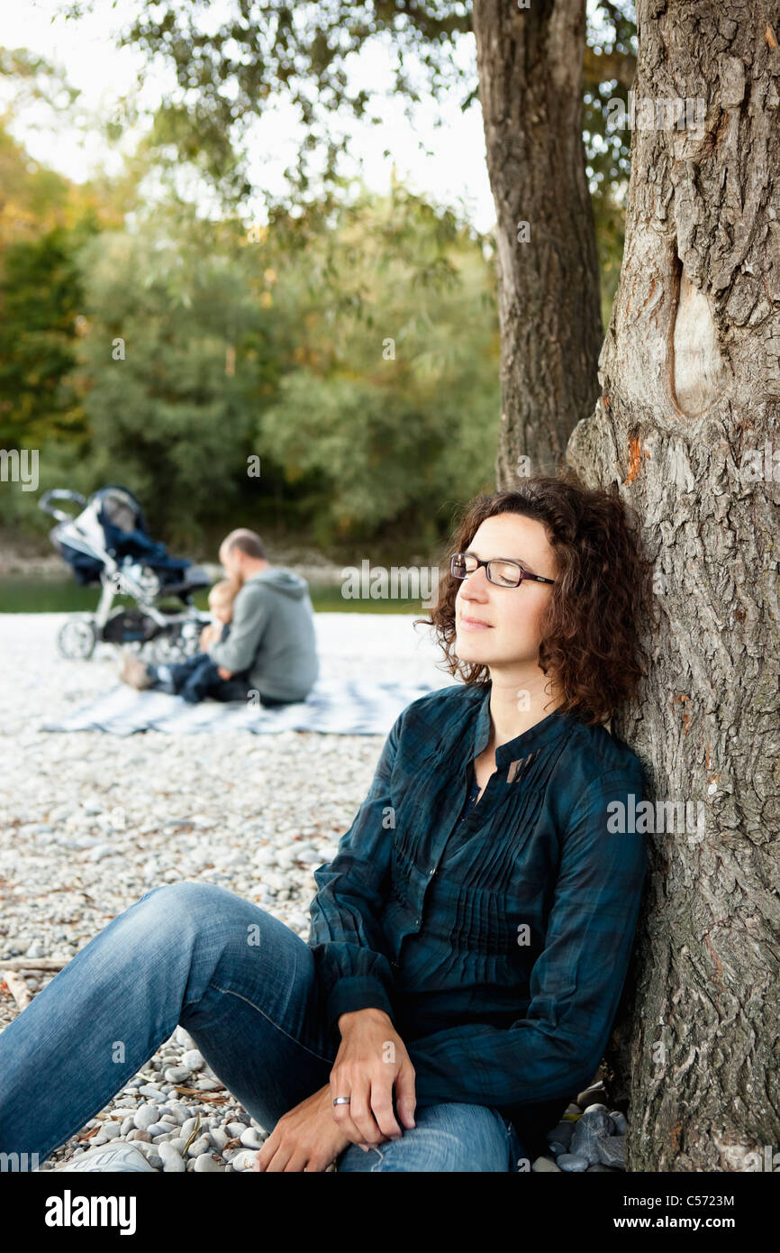 Mother resting by tree away from family Stock Photo - Alamy