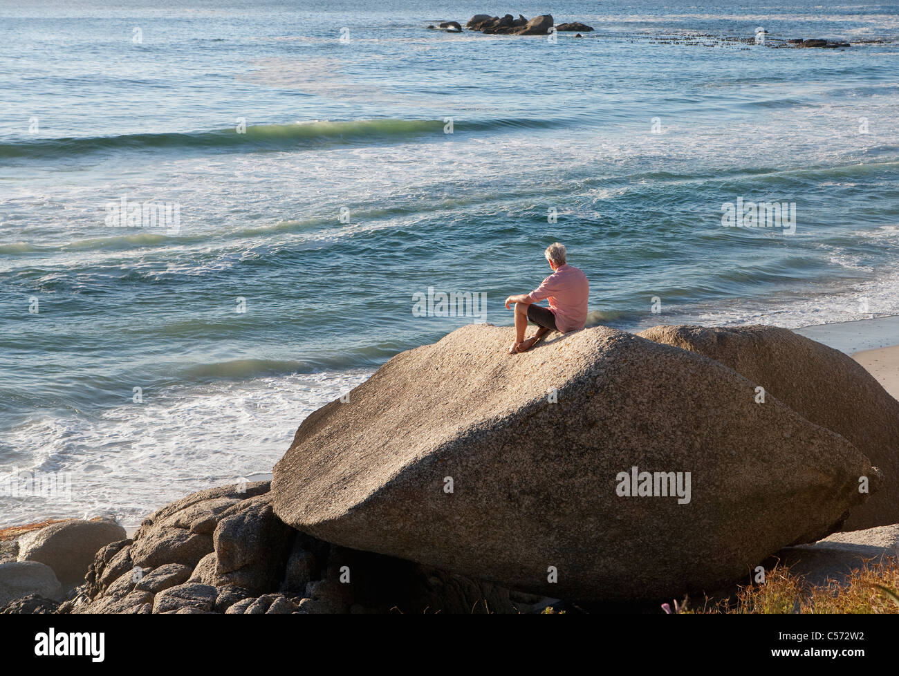 Man sitting on boulder on beach Stock Photo - Alamy
