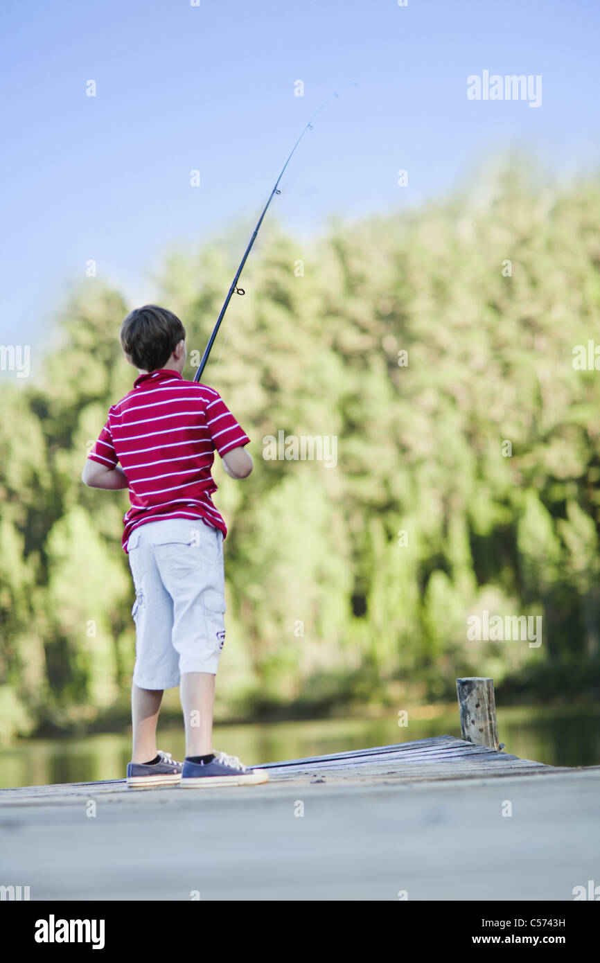 Boy with fishing rod on jetty over lake Stock Photo - Alamy