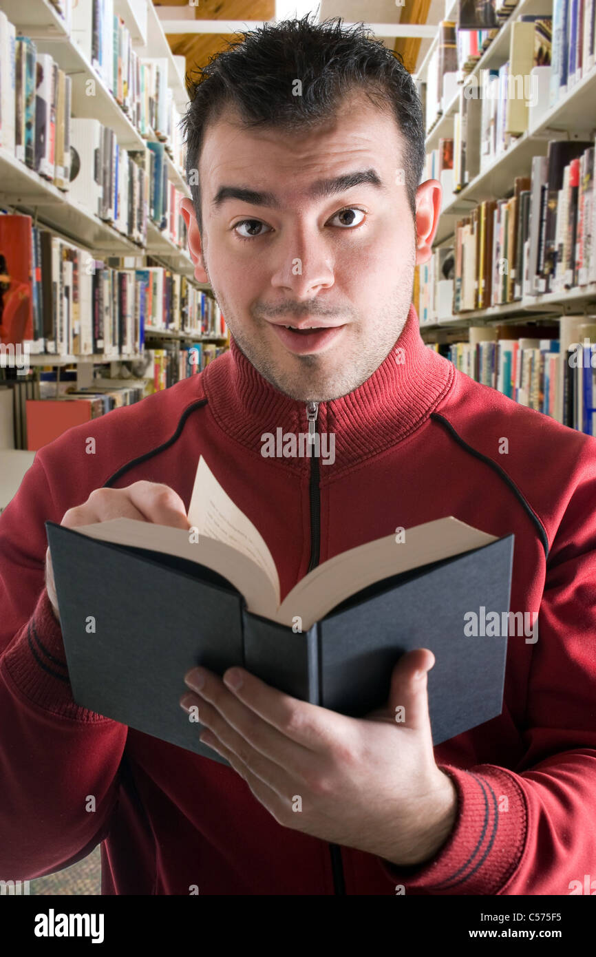 A young man looking at a book in the aisles of shelves at the library ...
