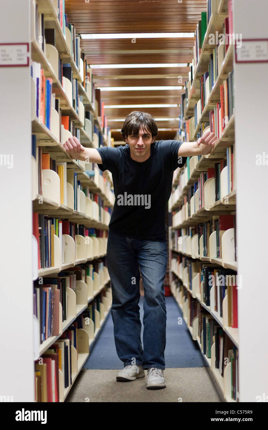 A young man standing in the aisles of the library book shelves Stock ...