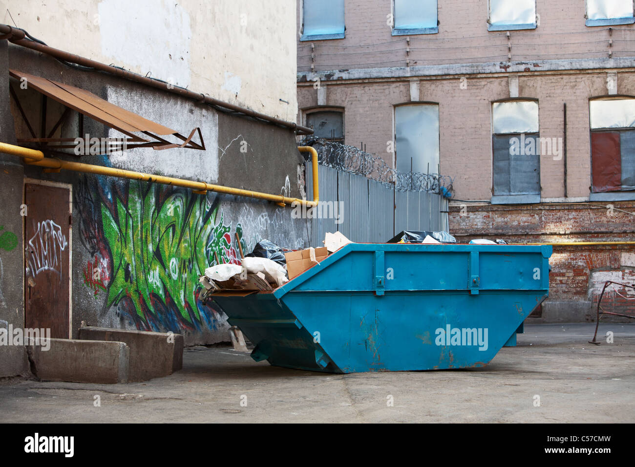 Blue dumpster filled with trash in alley Stock Photo - Alamy