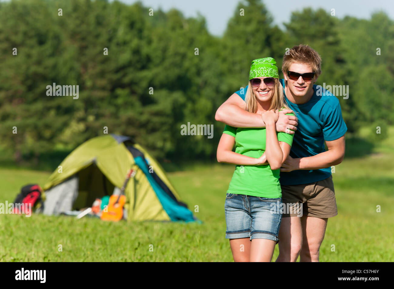 Young camping couple hugging in summer countryside tent in background ...