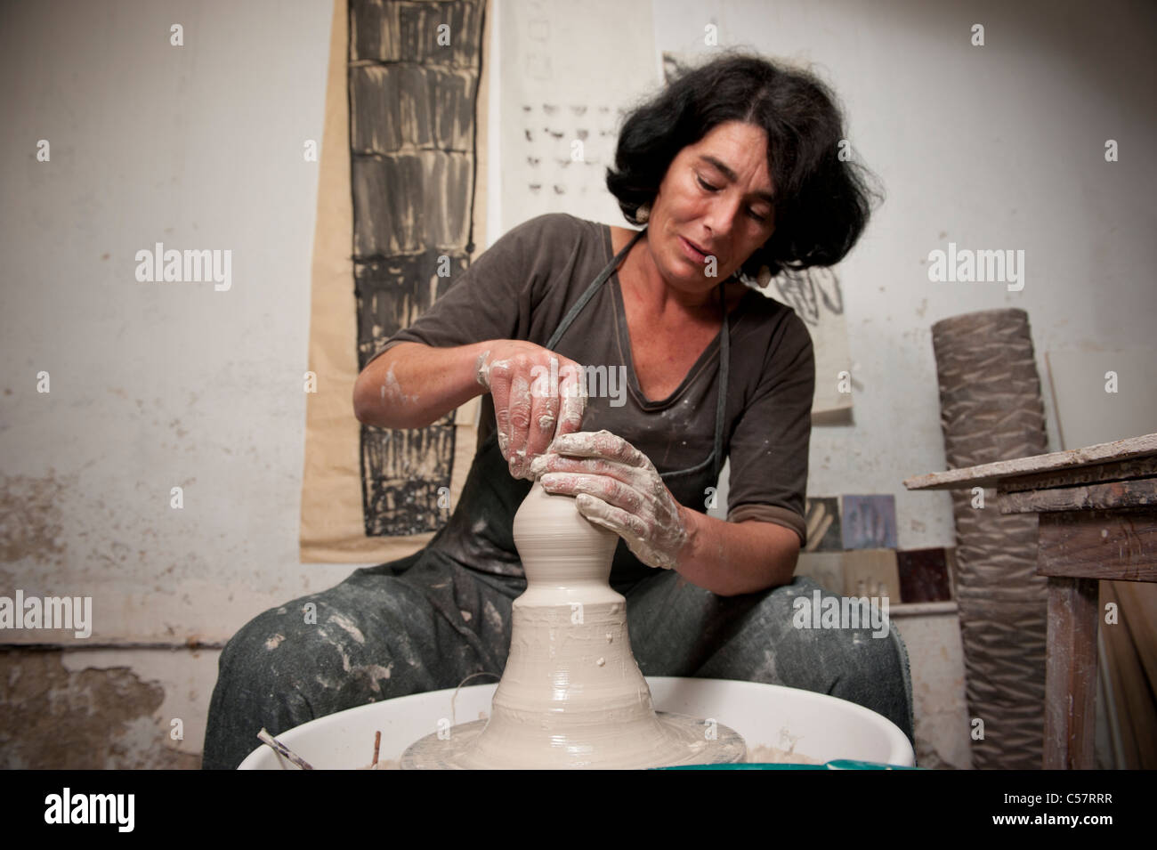 Female ceramicist using a Potter's wheel to work on a ceramic piece in ...