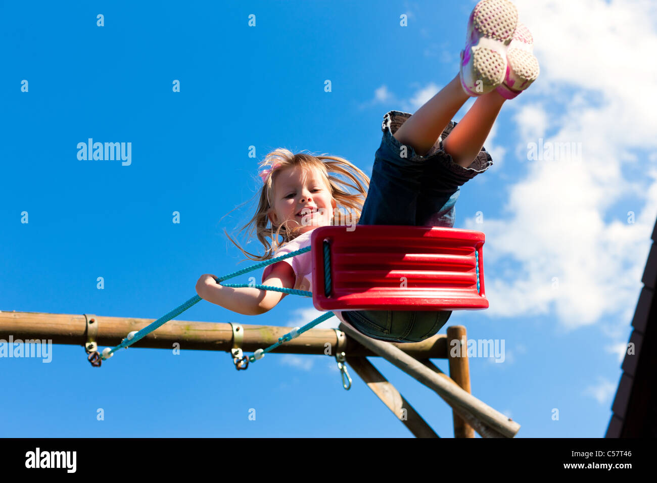 Little girl child sitting on a swing in the garden playground; she has ...