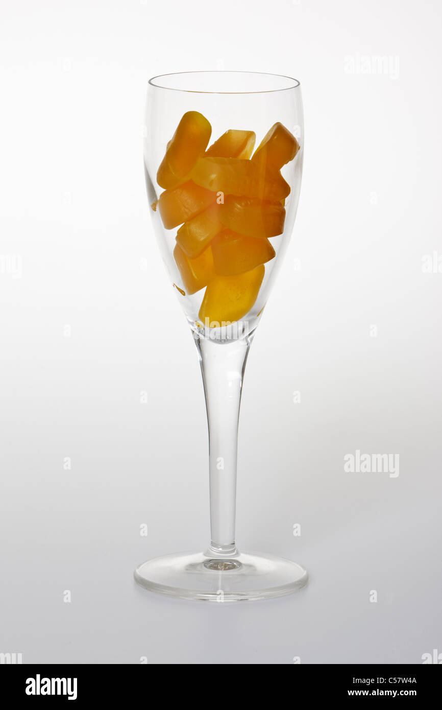 Wine glass filled with yellow wine gums against a plain white ...