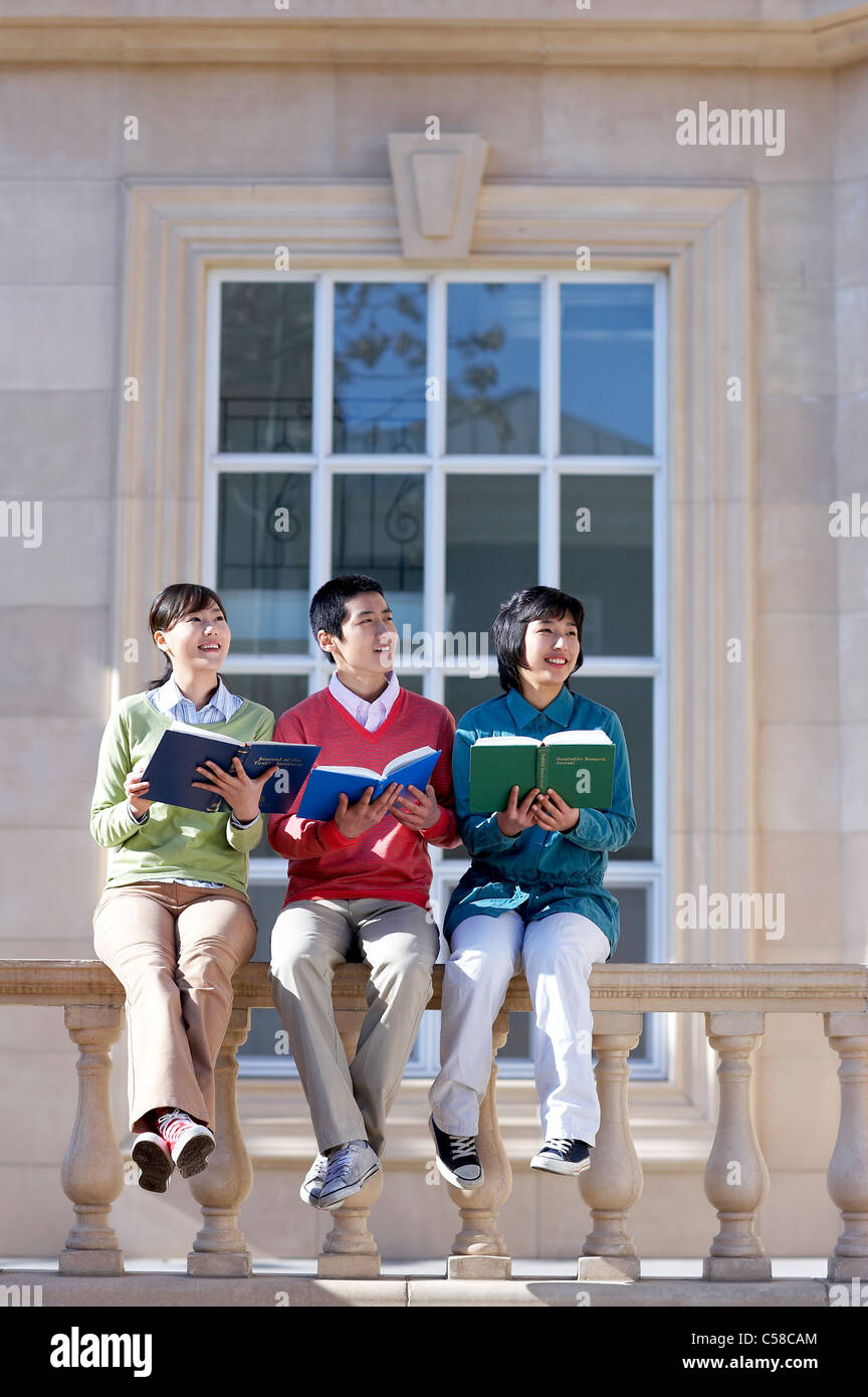 Teens sitting on railing in college, reading book Stock Photo - Alamy