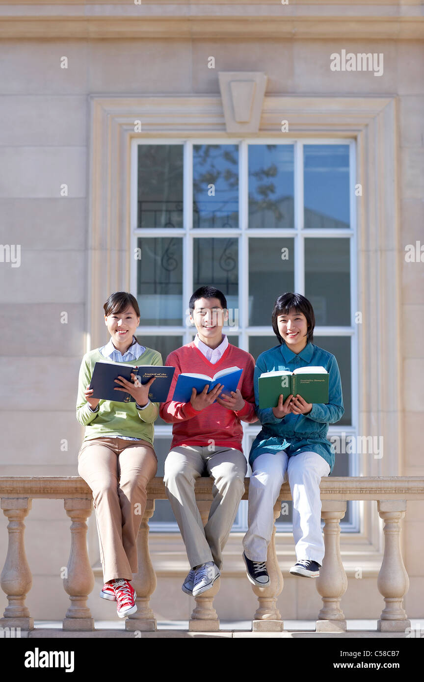 Portrait of teens sitting on railing in college, reading book Stock ...