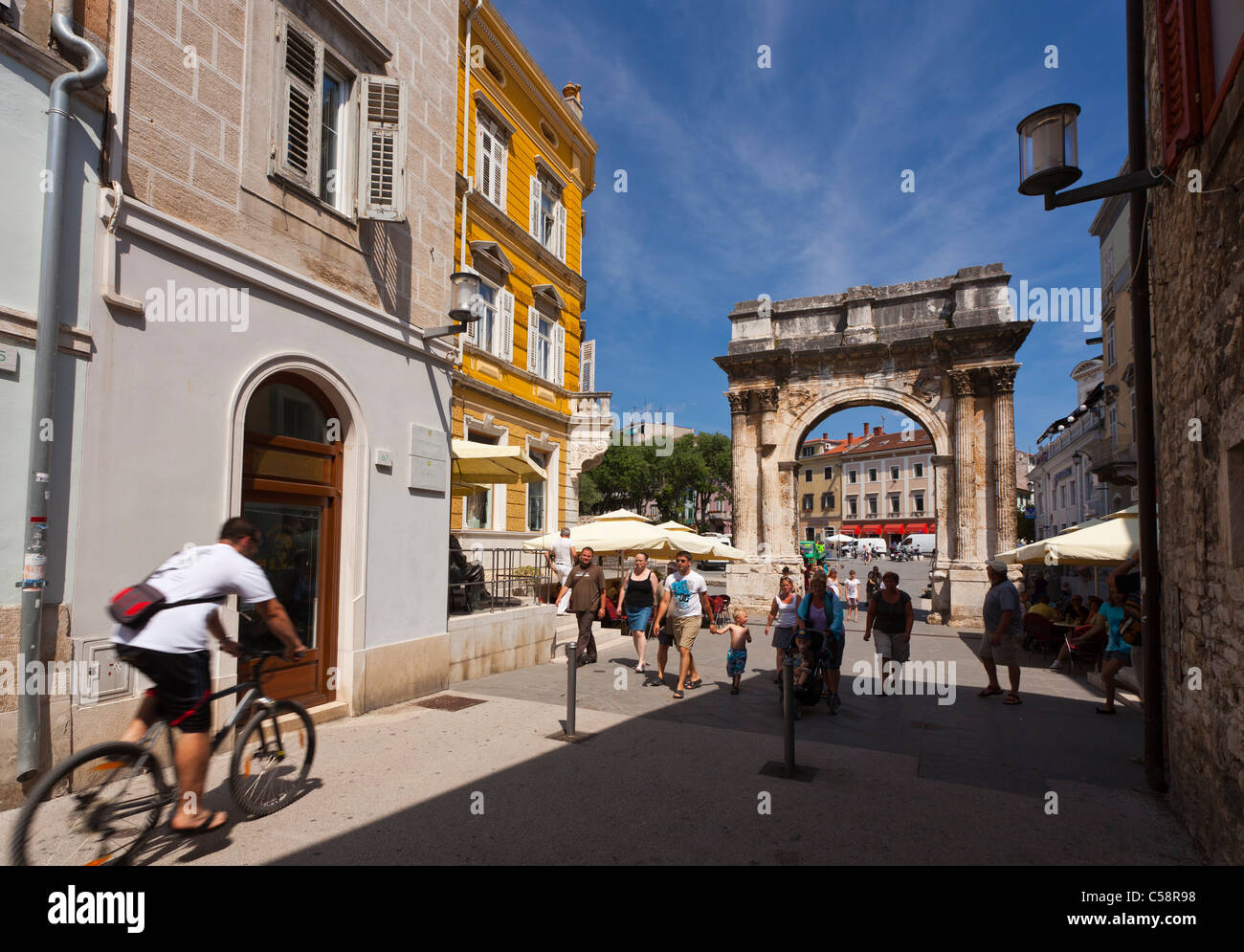 A cyclist and pedestrians passing through the "Golden Gate" of Pula ...