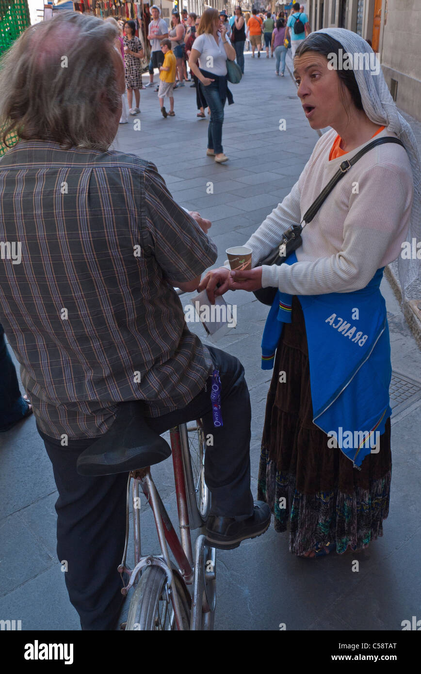 A Roma (Gypsy) woman begs a man on a bicycle for money in Florence ...