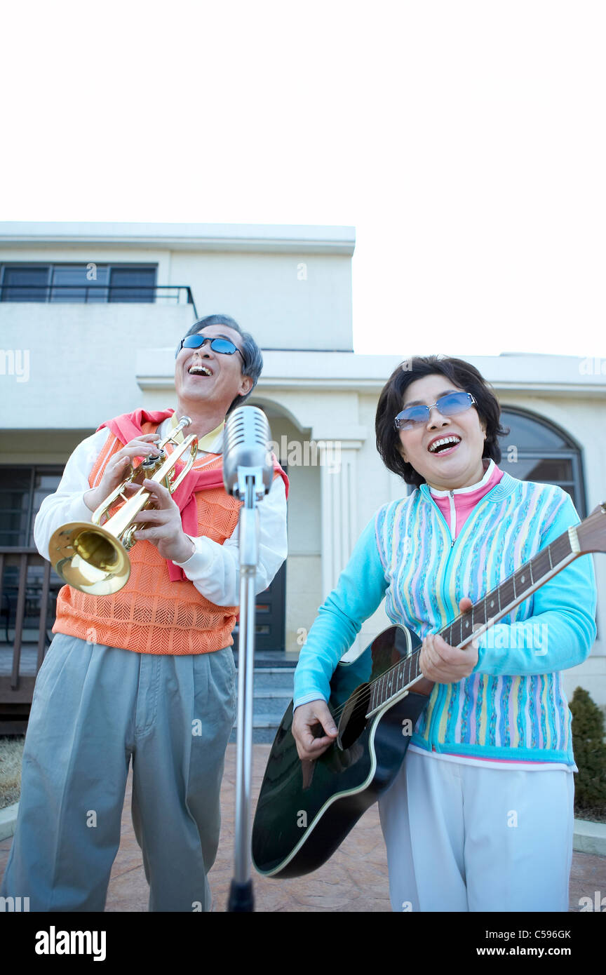 Senior couple standing by house with musical instrument Stock Photo - Alamy